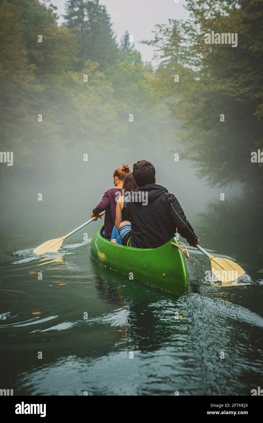 Back view of a green canoe in a misty and foggy river between the trees ...