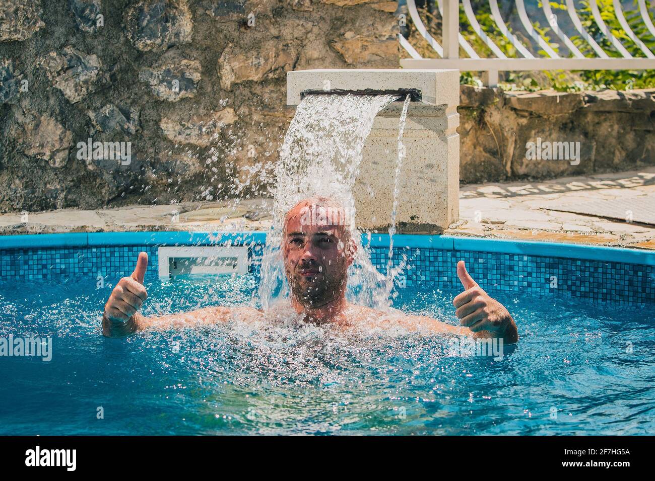 Young caucasian male with bald head enjoying a flow of water fountain ...
