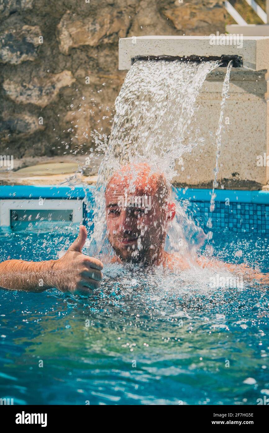 Young caucasian male with bald head enjoying a flow of water fountain ...
