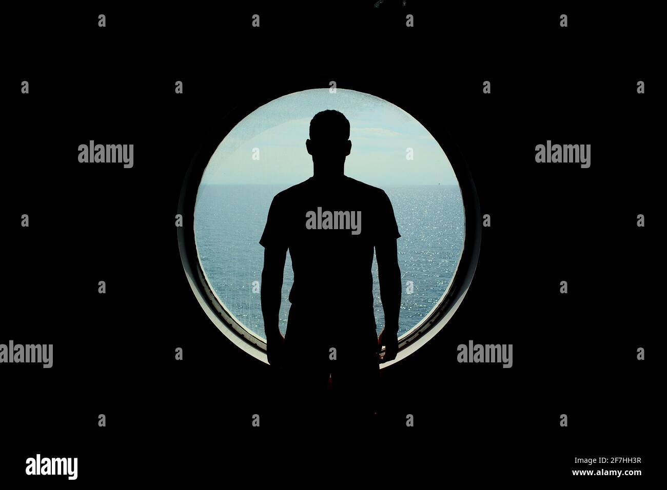 Silhouette of a man looking towards the sea through a large dirty round ...