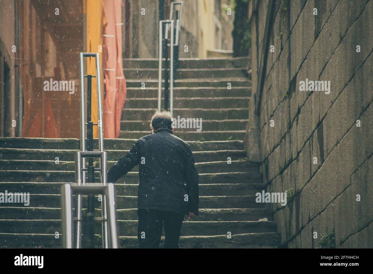 An unknown older man walking up the old stone stairs during rain and ...
