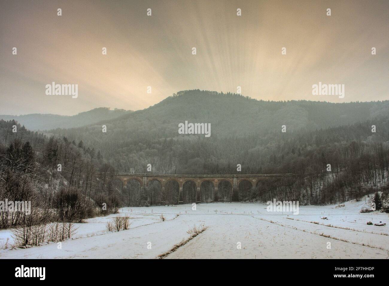 Old railway viaduct in winter with sun rays shining above the hill ...