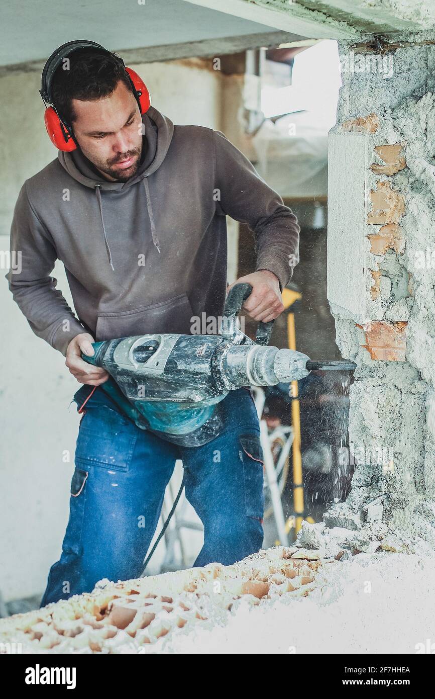 A person using an automatic hammer demolishing a house wall during a ...
