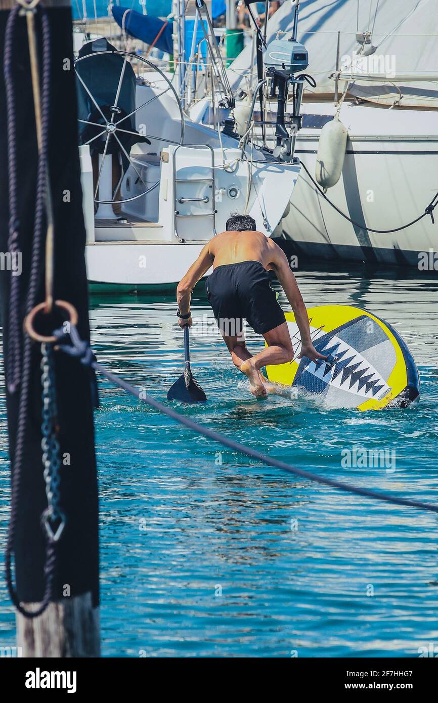Back view of a man falling from a SUP board into the sea in a marina ...