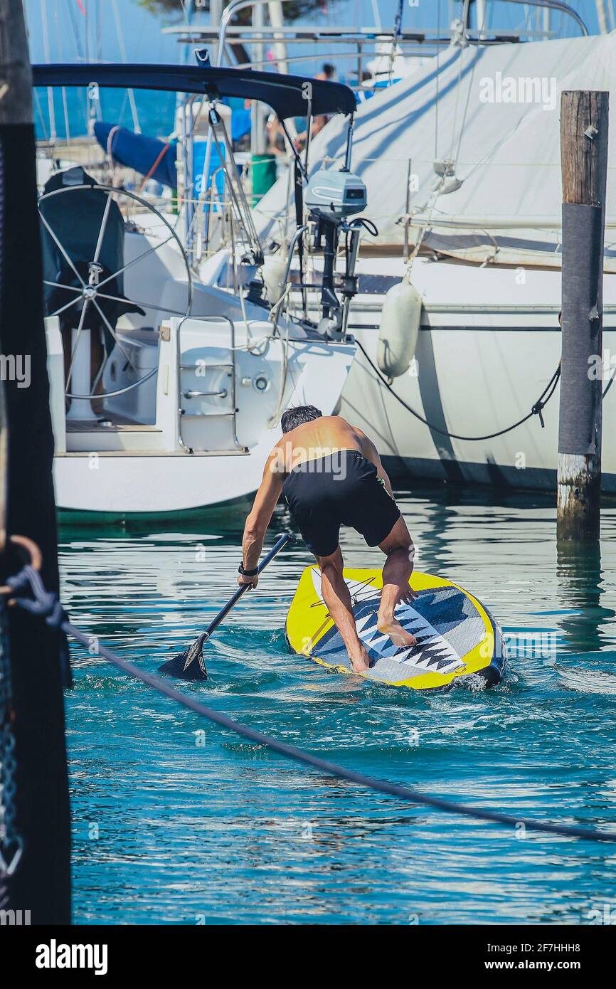 Back view of a man falling from a SUP board into the sea in a marina ...
