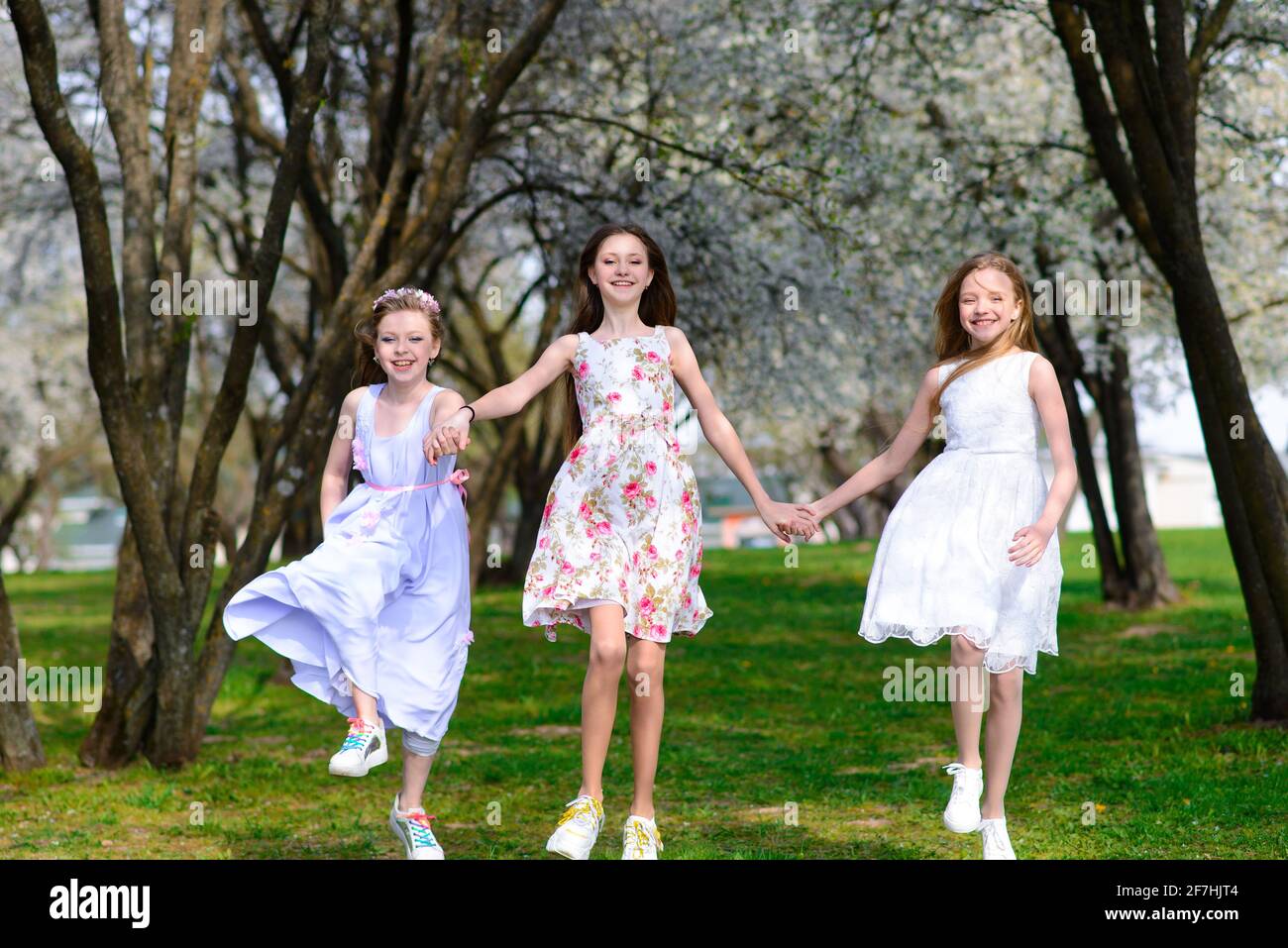 Three beautiful girls in retro dresses for a walk in a flowered garden ...