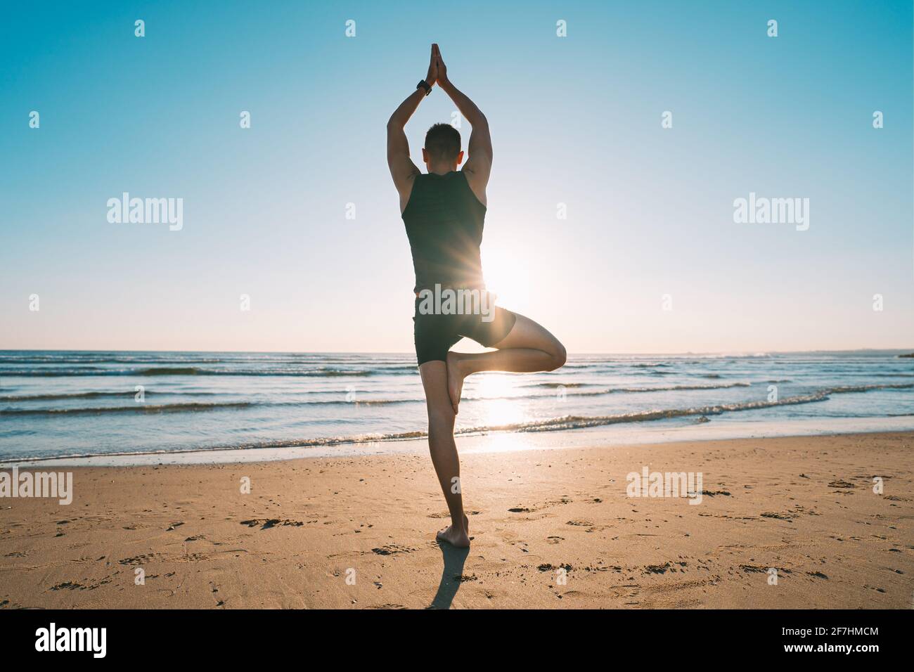 Man practicing yoga on the beach with ocean view at sunset or sunrise ...