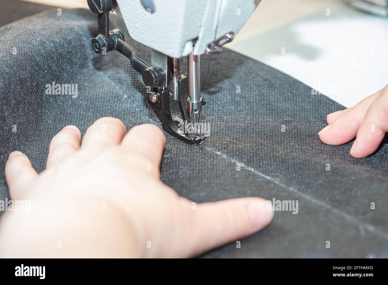 A woman seamstress sews a black cloth on an industrial sewing machine ...