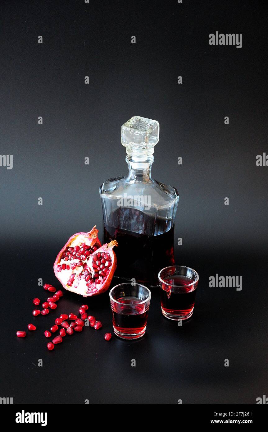 Homemade pomegranate liqueur in a glass decanter and two glasses, next to a broken fruit and ...