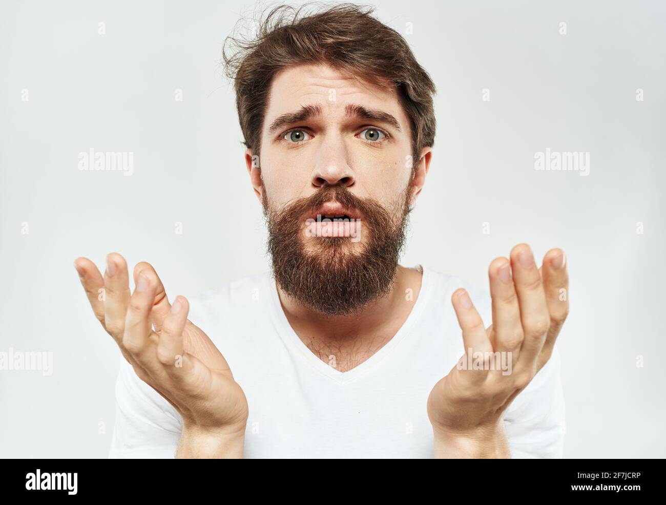 A man gestures with his hands on a light background in a white t-shirt ...