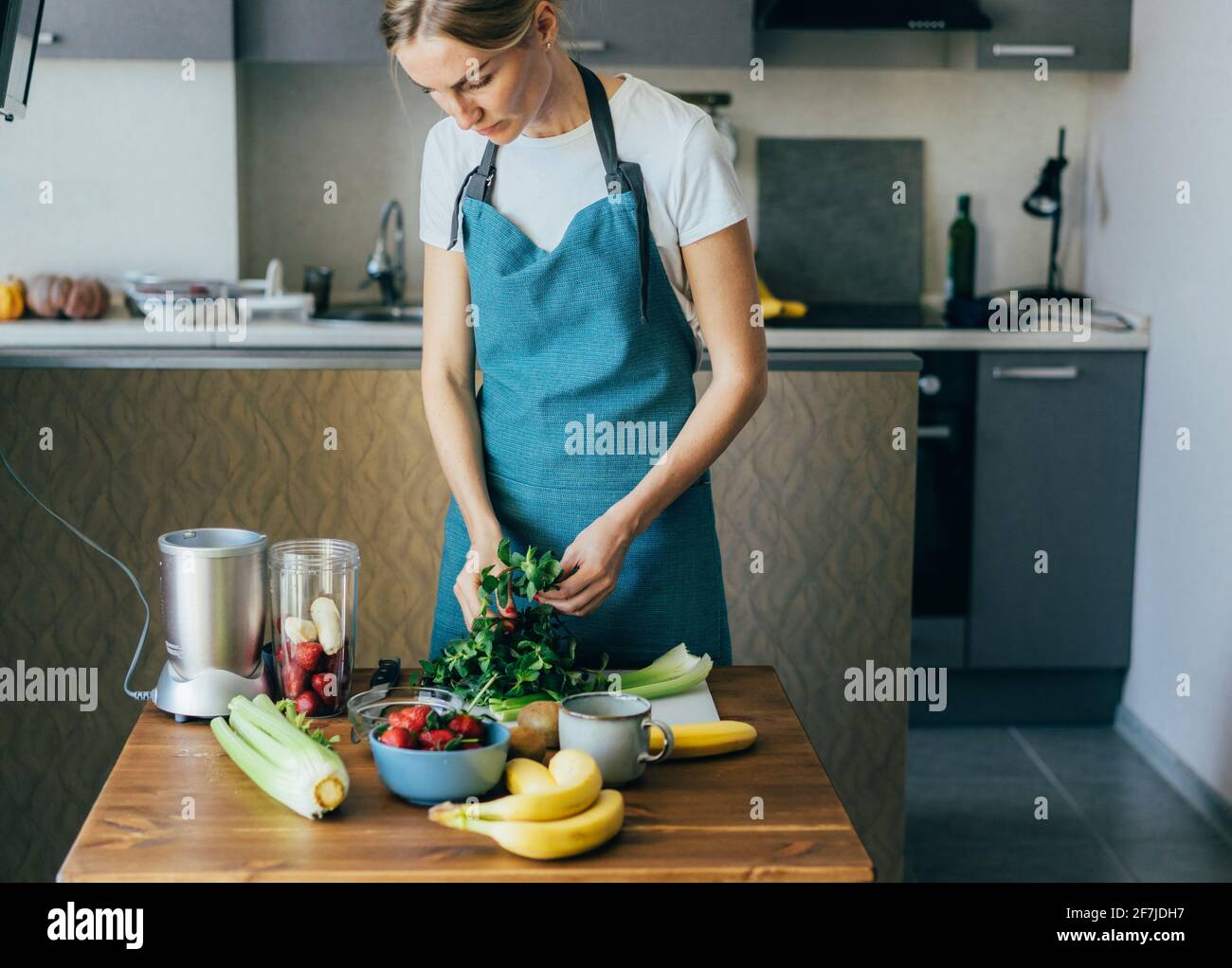 A female chef in a blue apron prepares a vegan fruit cocktail in her ...