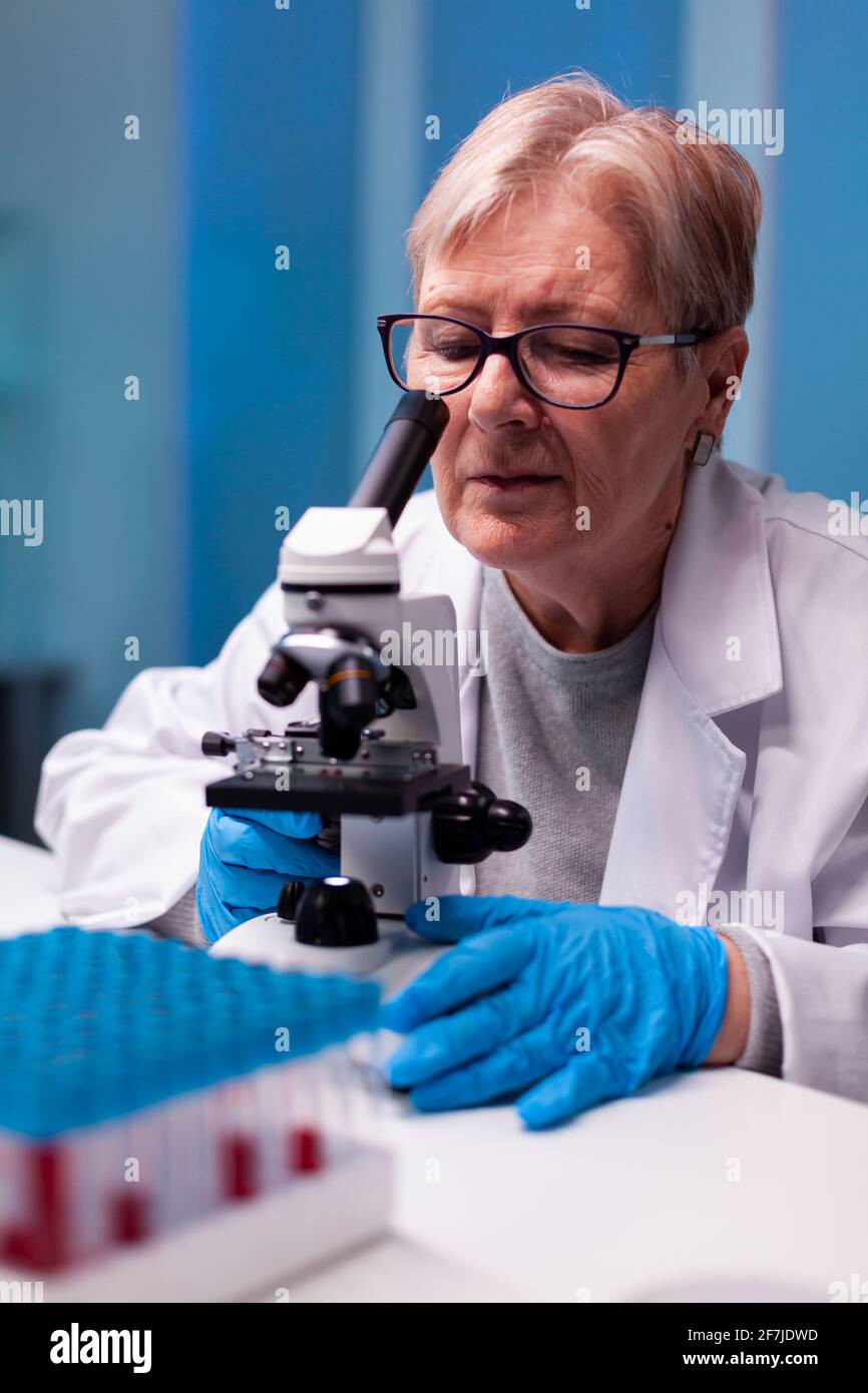 Senior scientist looking through microscope at sample in biology lab ...