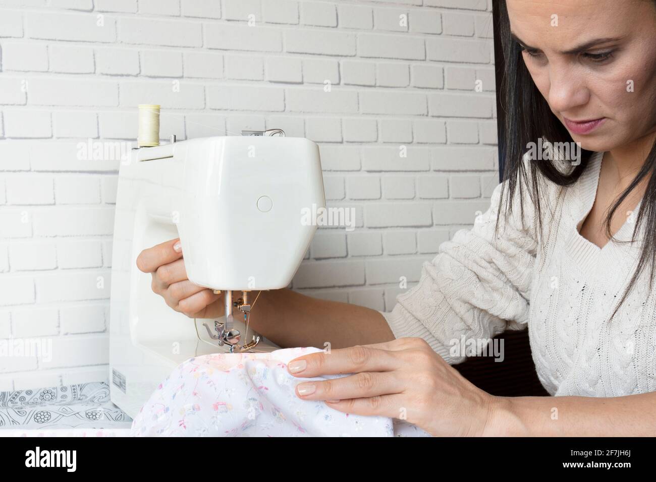 beautiful brunette young woman sews dress with the sewing machine ...