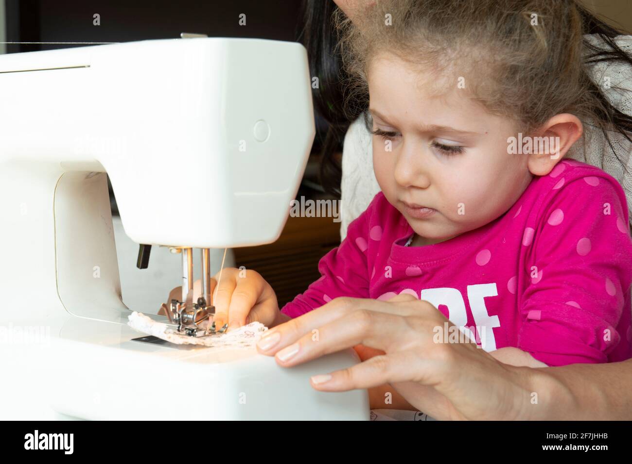 little girl is learning from her mother to use a sewing machine ...