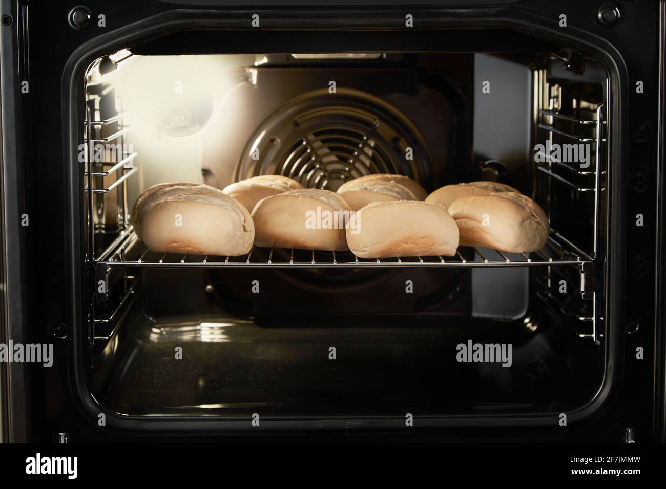 Metal rack with half baked bread buns loaded in modern fan oven for ...