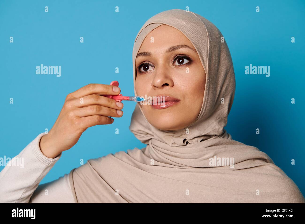 Closeup of beautiful Muslim woman in hijab holding a syringe with ...