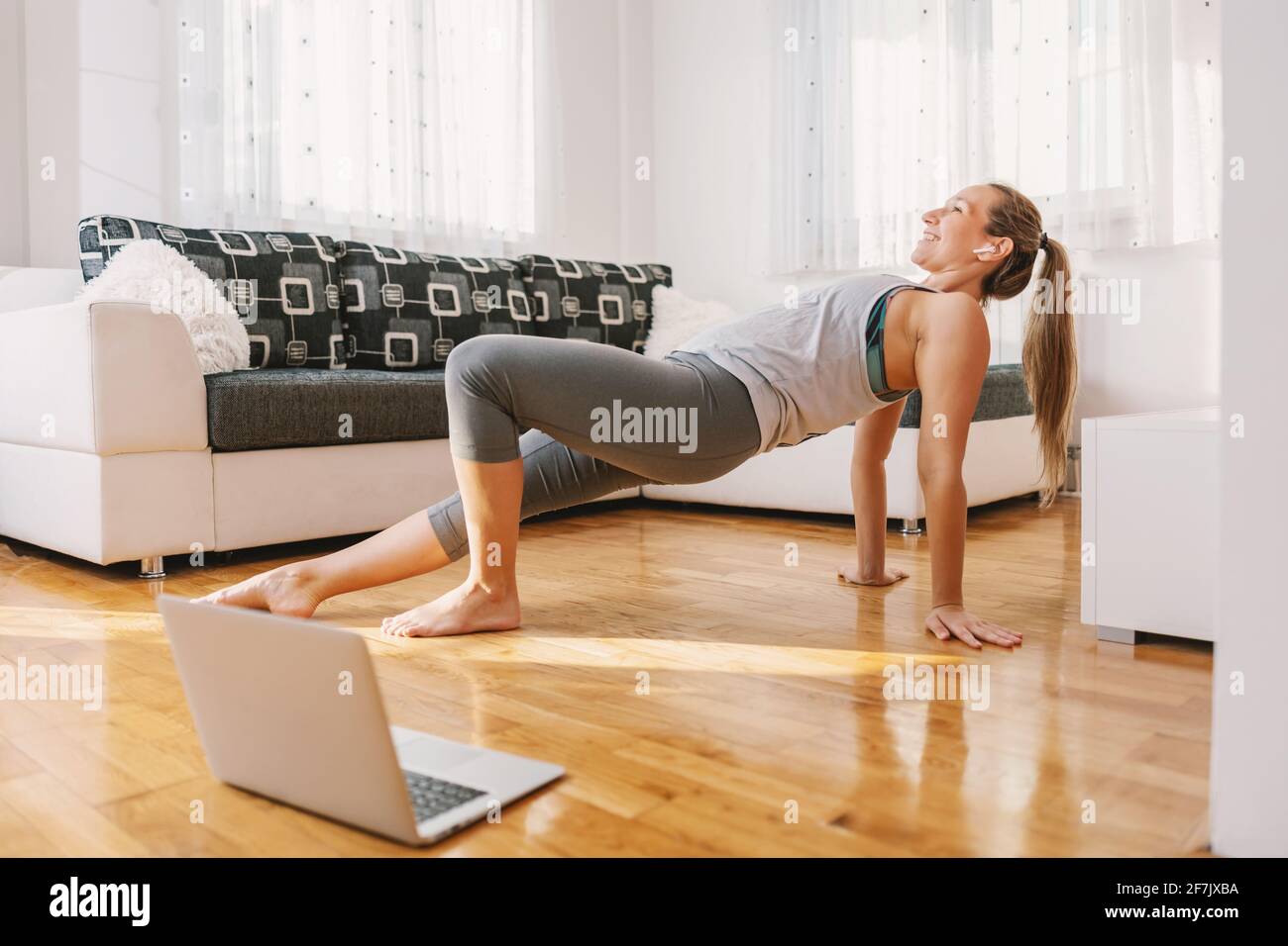 Smiling muscular fitness instructor sitting at home on the floor and ...