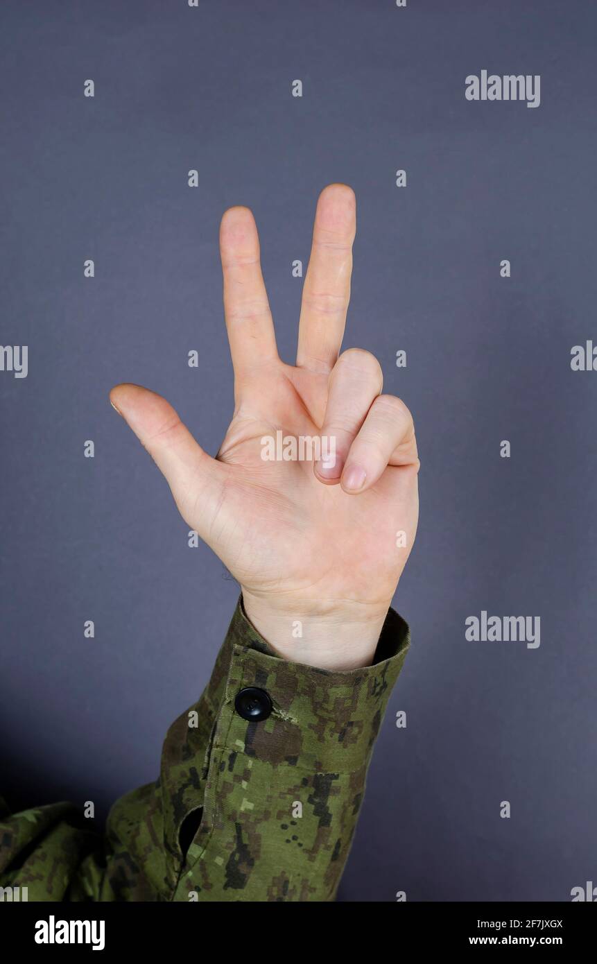 Hand in camouflage shows gesture with his fingers on gray background ...