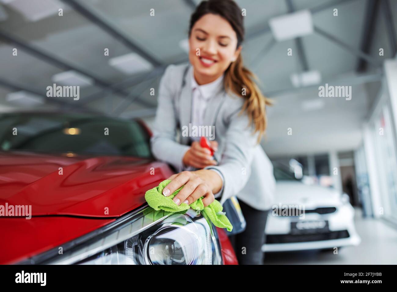 Smiling tidy female car seller rubbing car with detergent and cloth ...