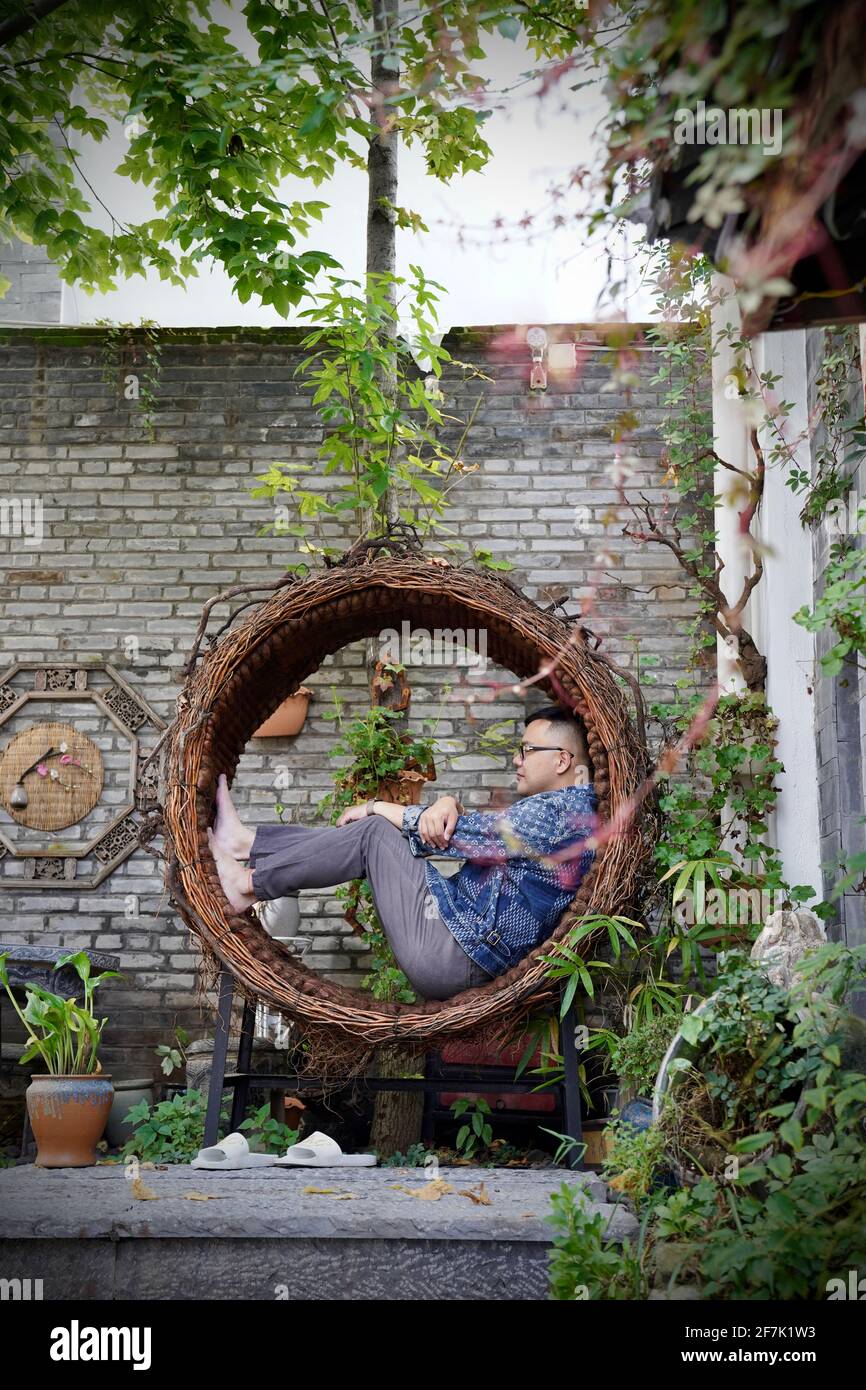 A young asian man is resting in a ratten cradle in round shape that ...