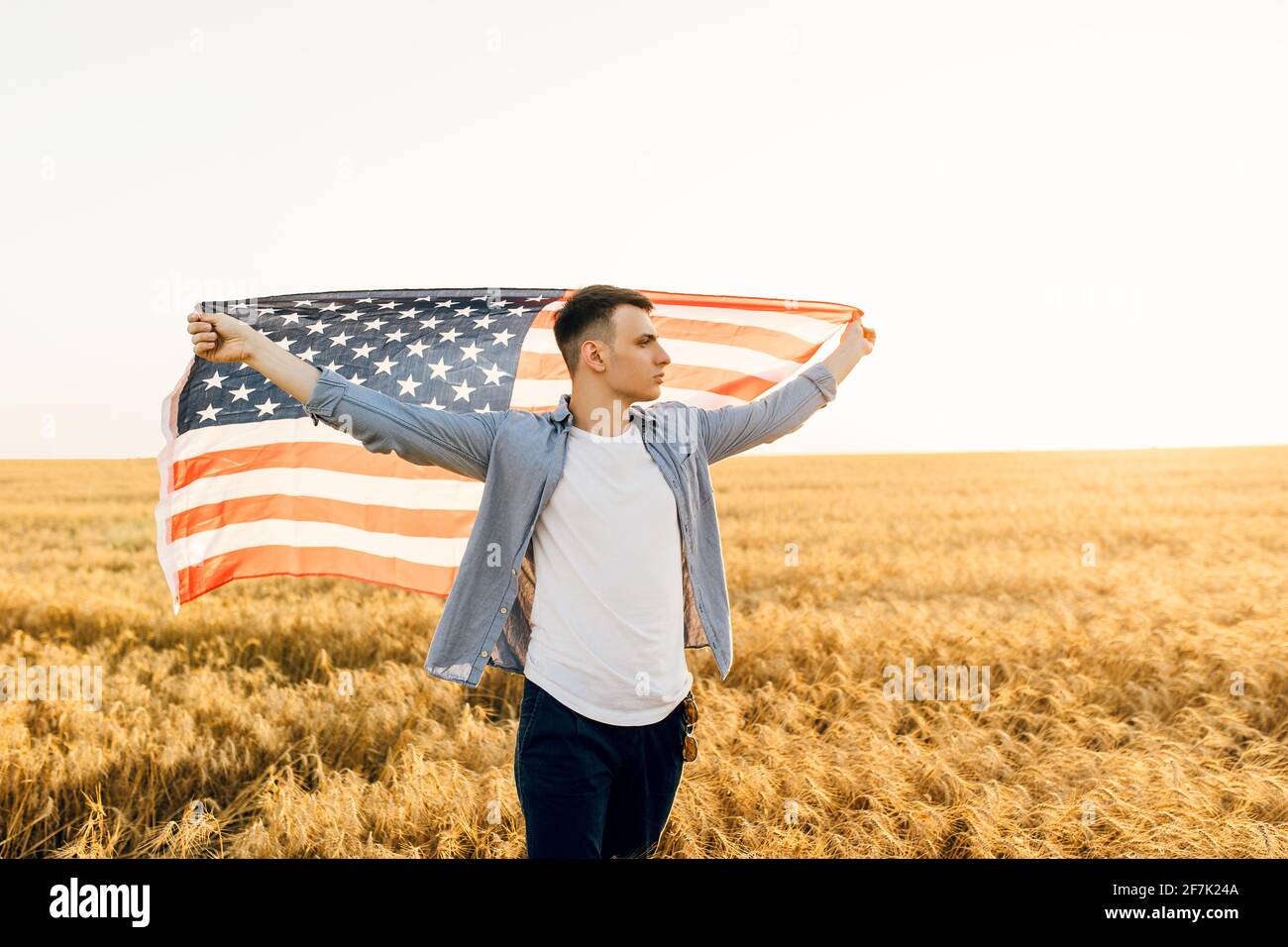 Young man holding American flag while standing on wheat field against ...