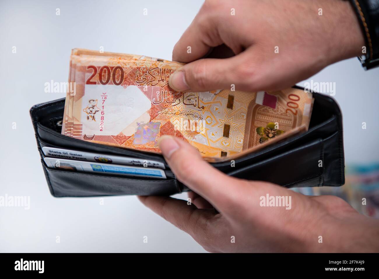 Men's hands holding wallet with Qatari notes. 200 Rial new notes ...
