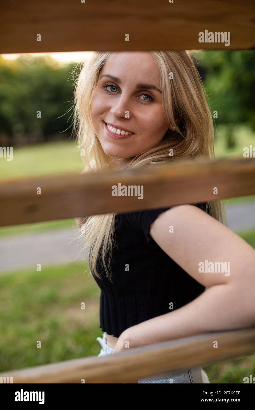 European young white model woman smiling in park leaning to a wooden ...