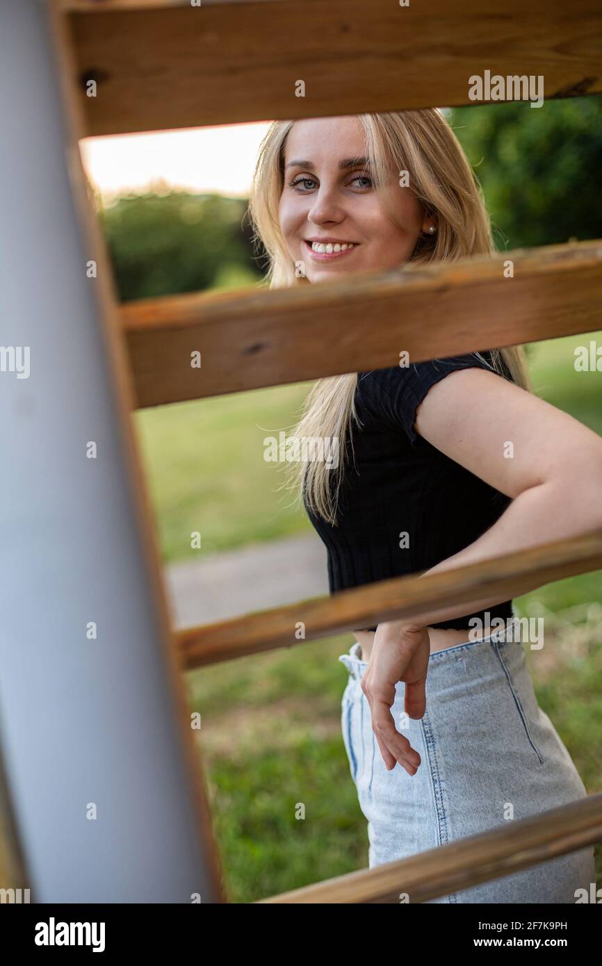 European young white model woman smiling in park leaning to a wooden ...