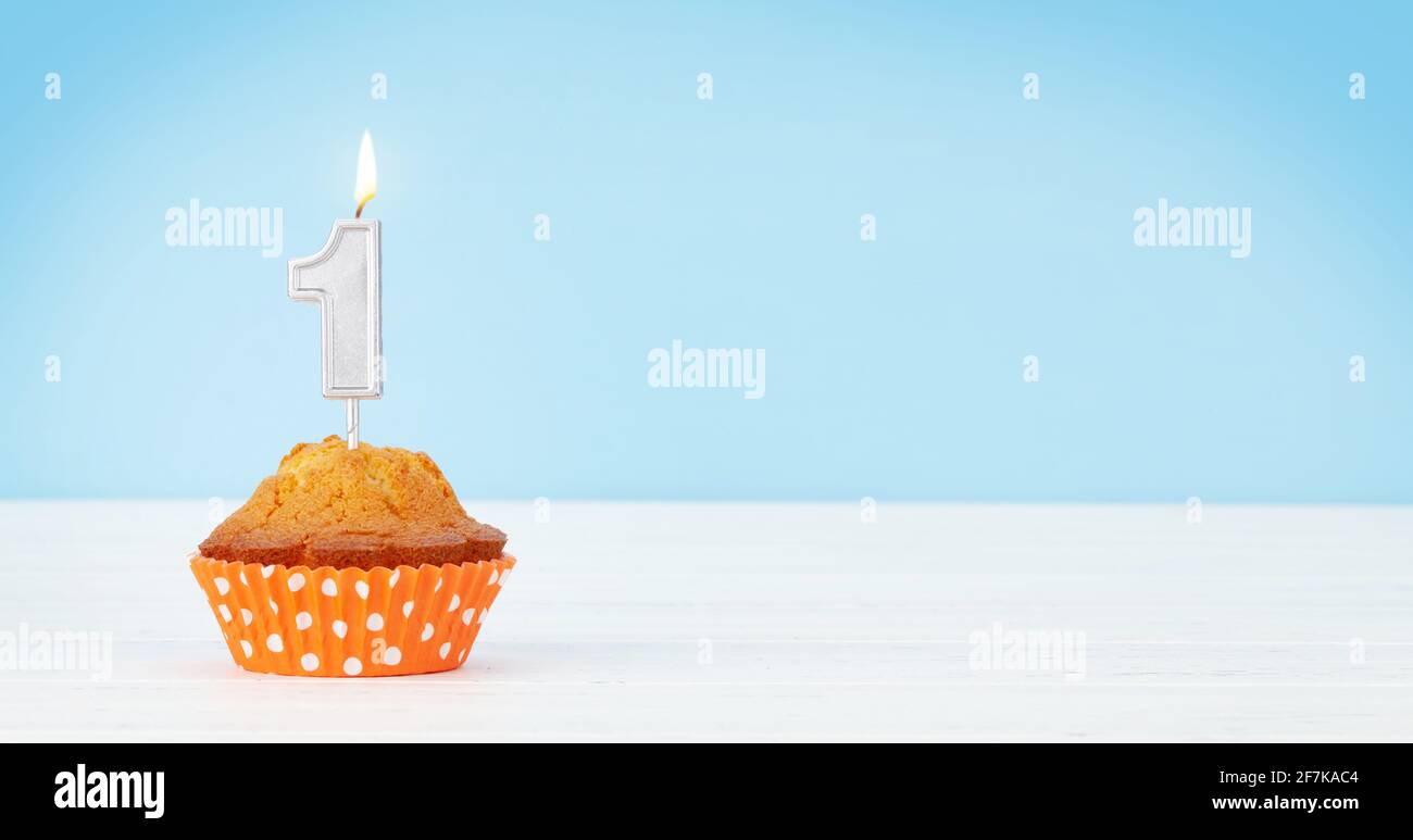 Birthday cupcake with number one burning candle over blue background ...