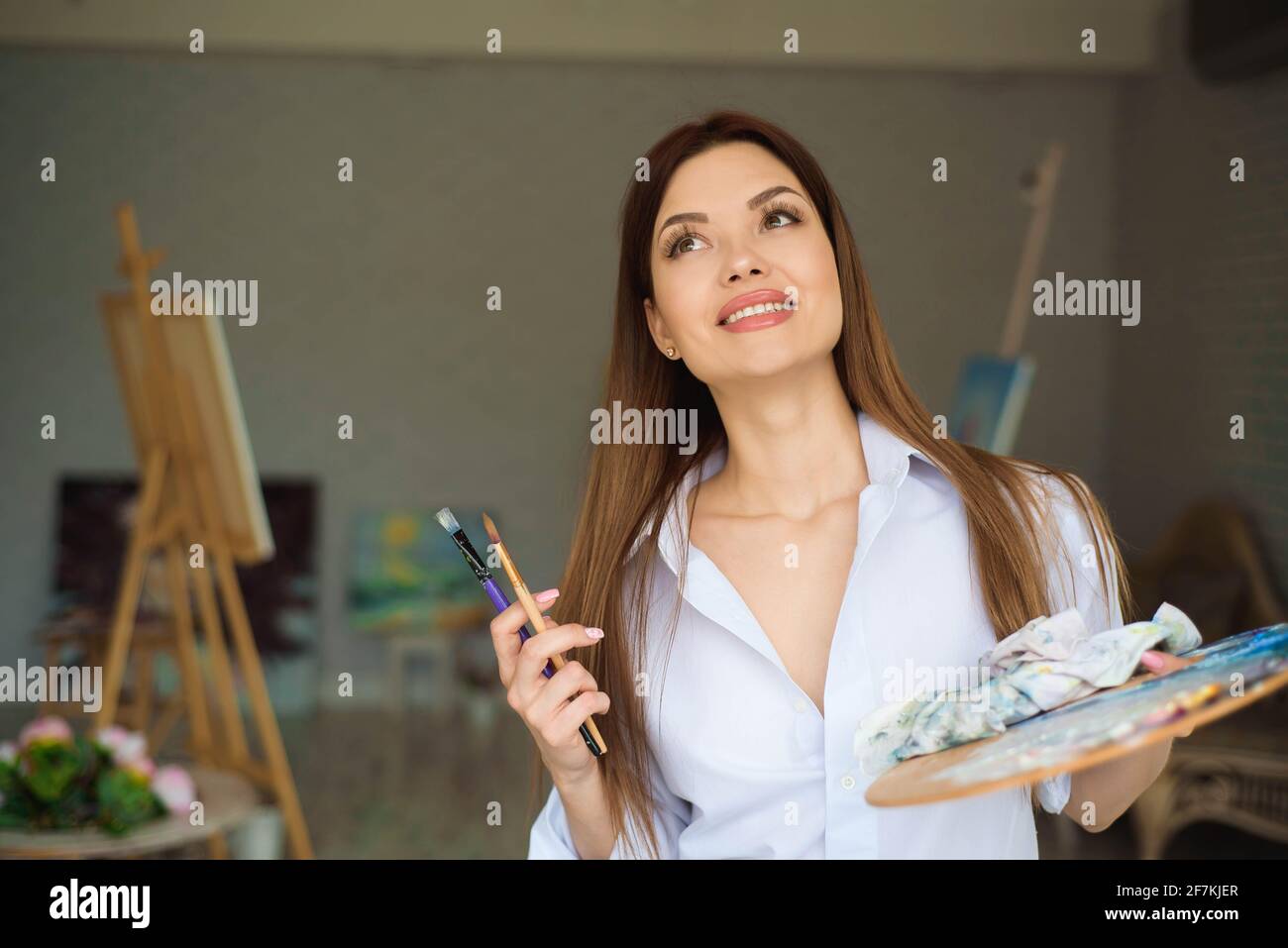 Portrait of talented young woman painting picture in art studio with ...