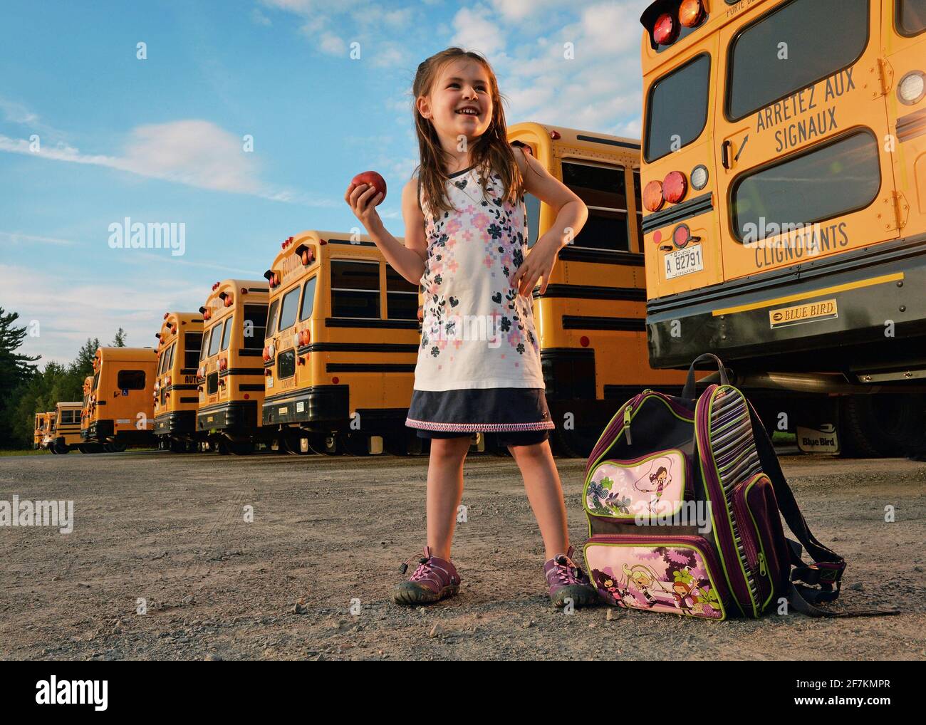 Little girl with an apple in her hand with school buses Stock Photo - Alamy