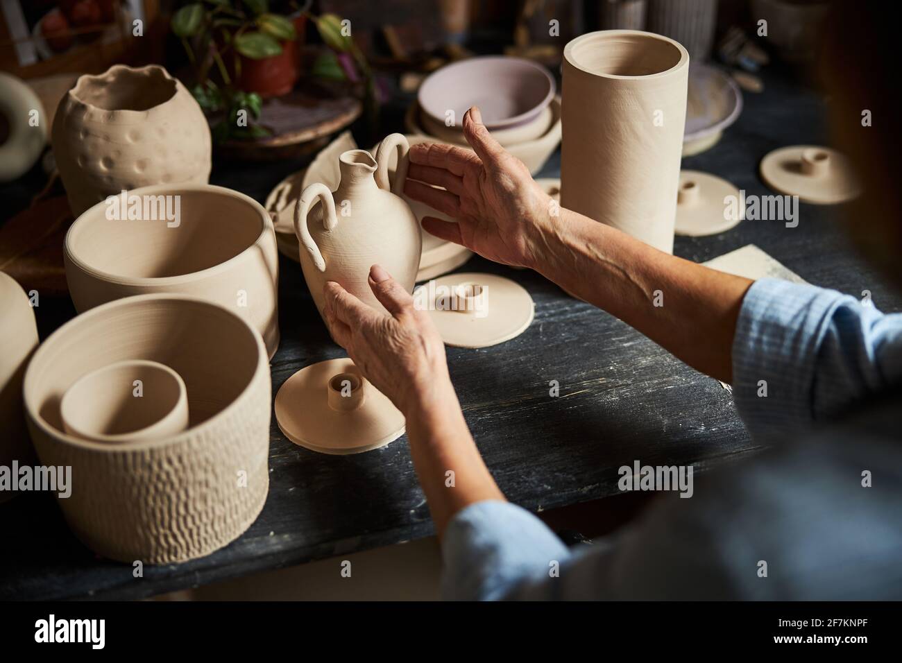 Female ceramic artist sitting at the table with pottery in workshop ...
