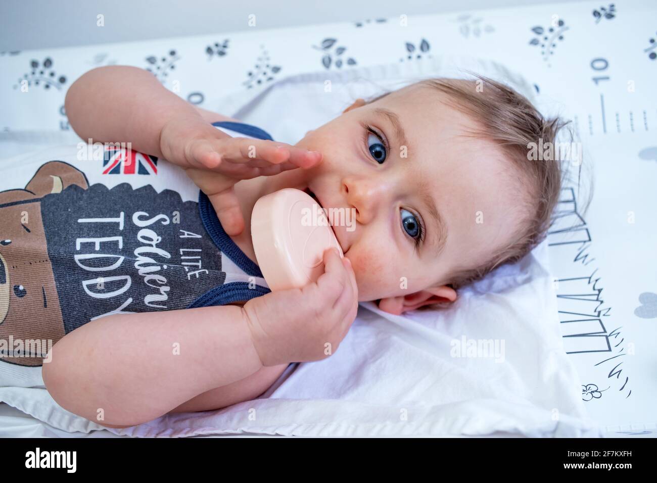 Baby boy on changing table putting a plastic lid in his mouth as a toy ...
