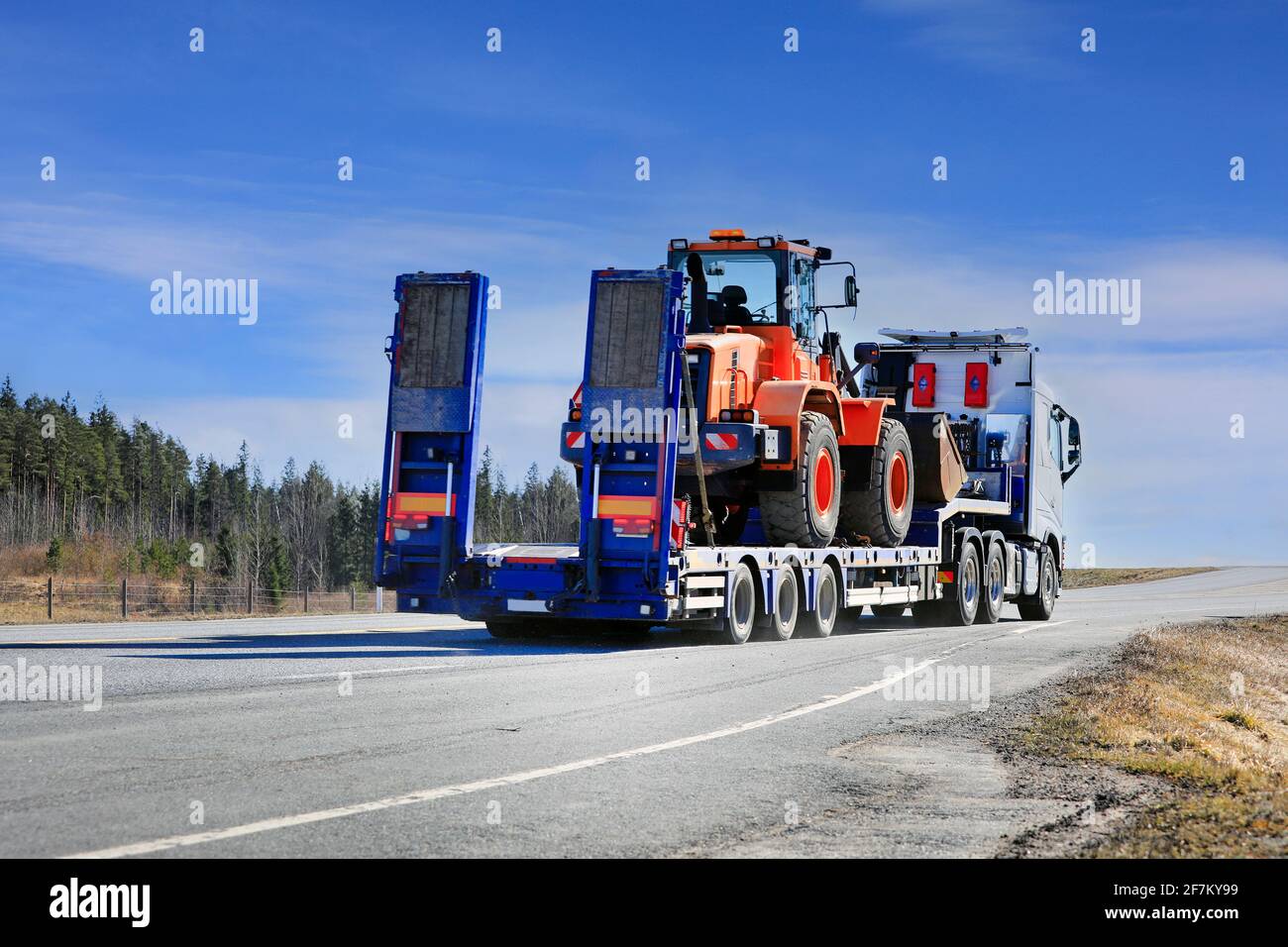 Semi trailer truck transporting wheel loader on highway on a beautiful ...