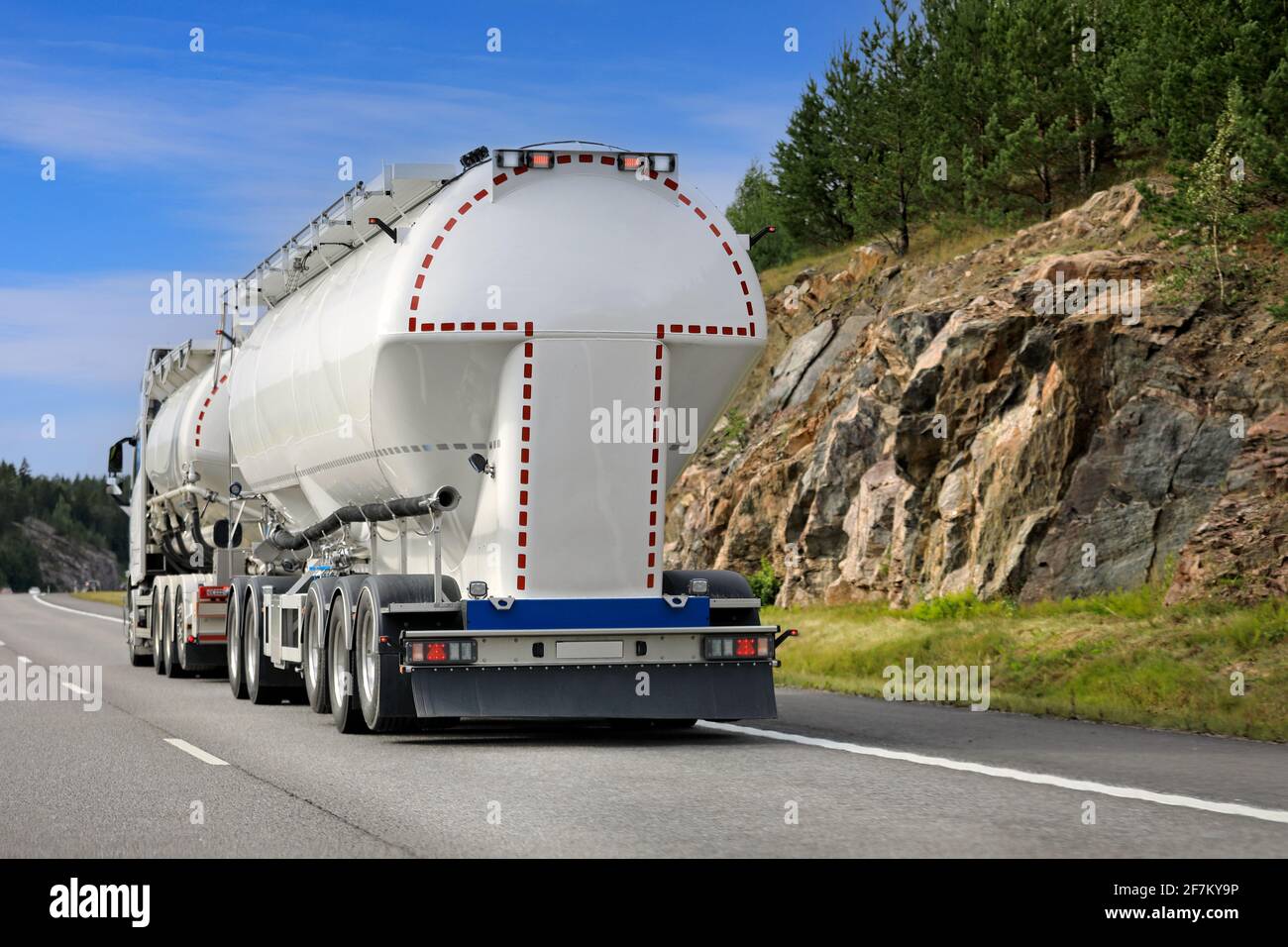White freight truck pulling white tank trailer on multiple lane highway ...