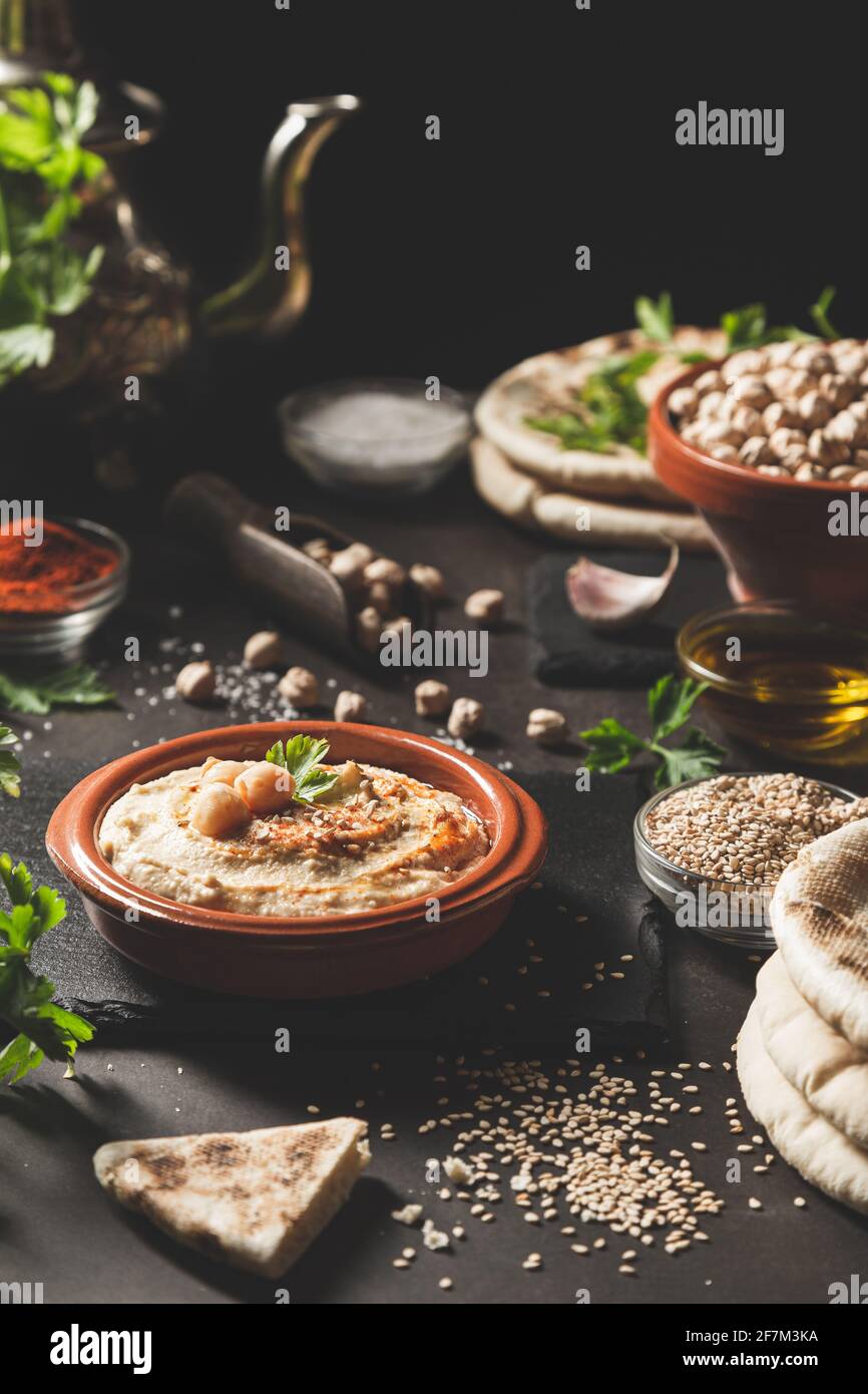 Classic hummus in a bowl with ingredients on dark background. Vertical ...