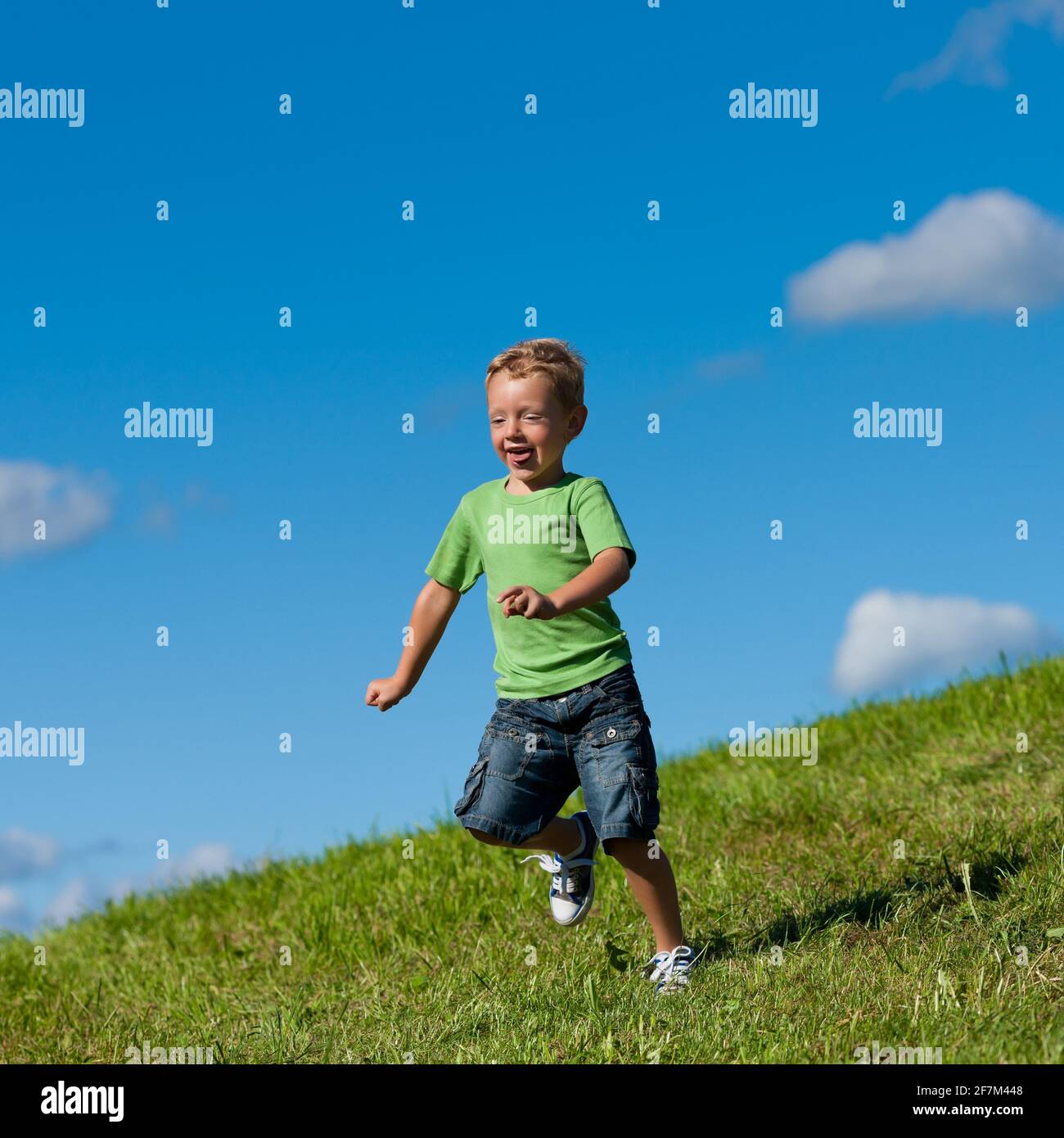 Little boy running down a meadow in a beautiful landscape in summer ...