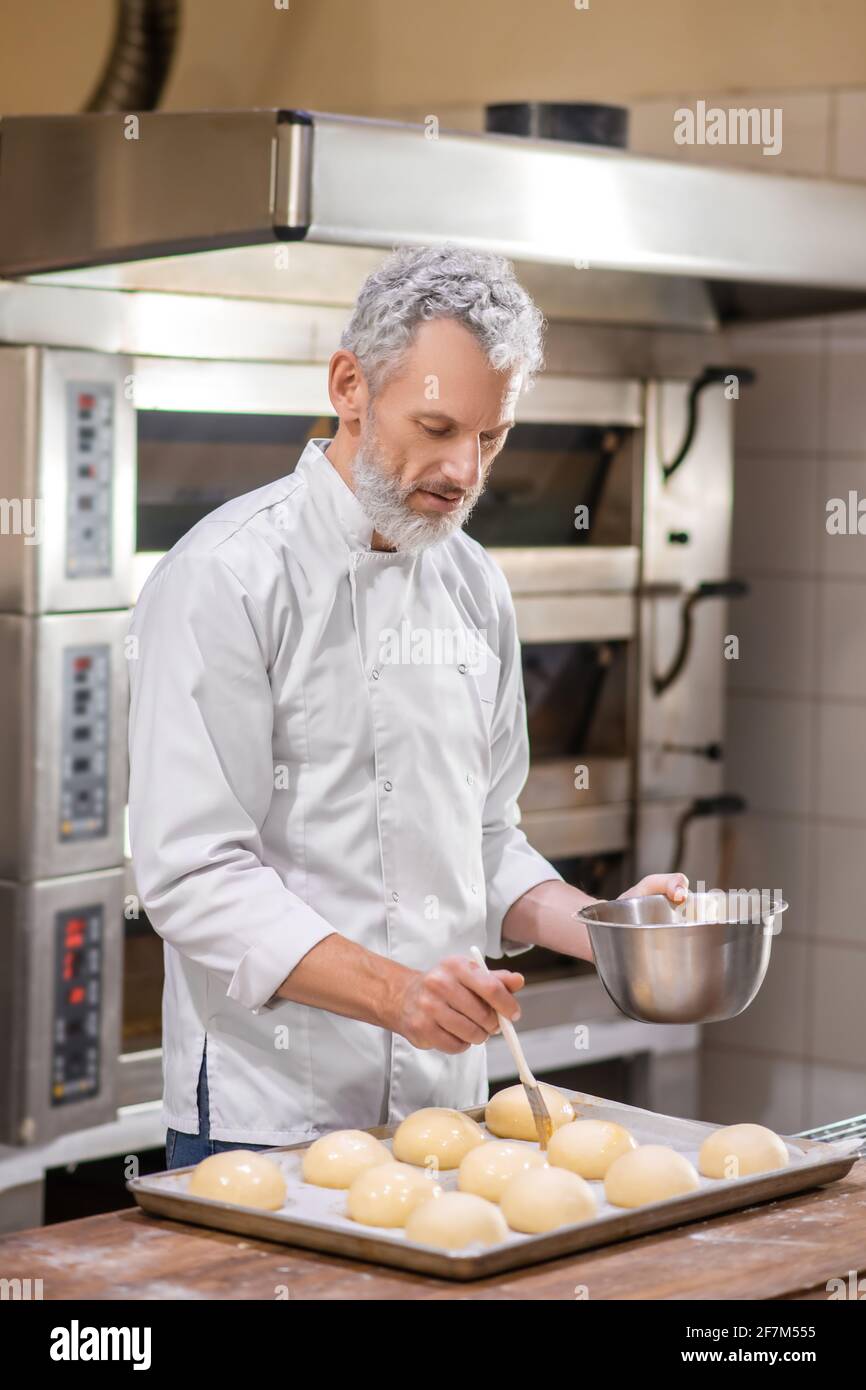 Man covering buns with special glaze Stock Photo - Alamy