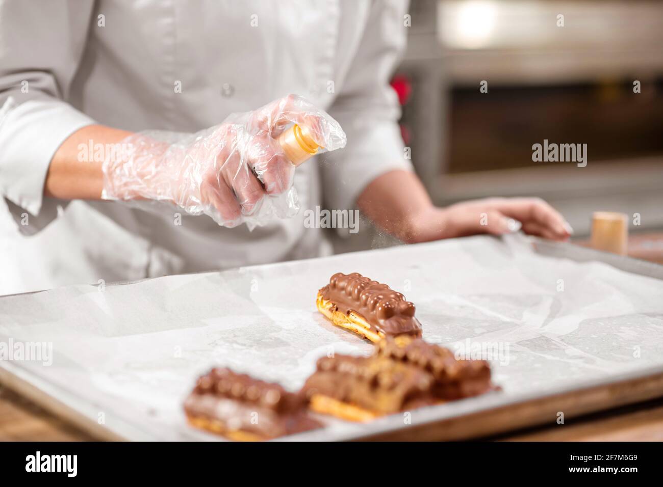 Hand with spray decorating ready-made eclair Stock Photo - Alamy