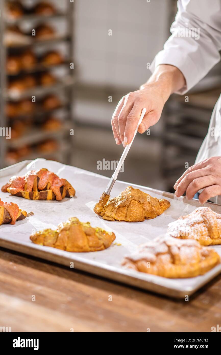 Pastry chefs hand with brush over tray of croissants Stock Photo - Alamy
