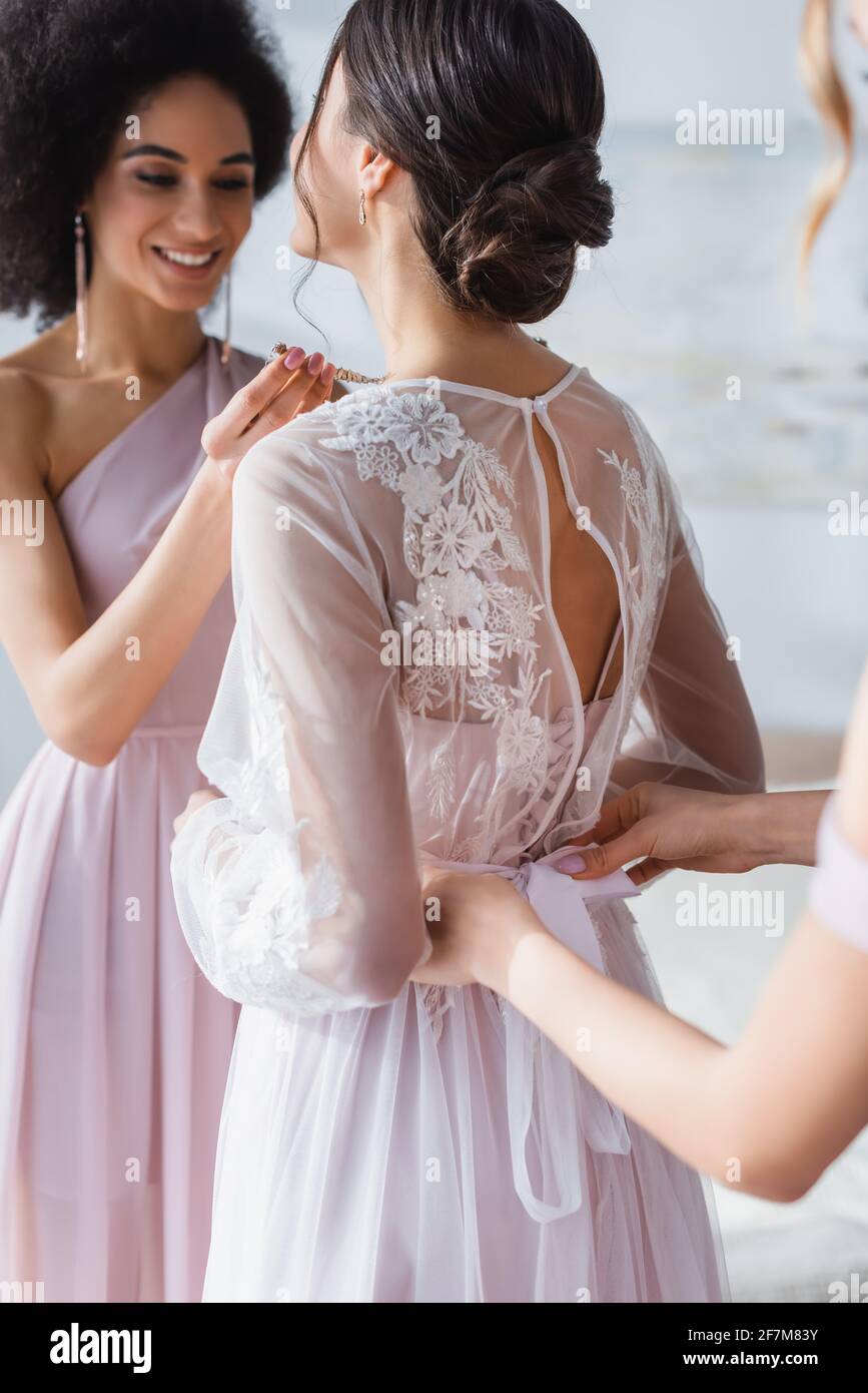 african american woman with friend preparing bride for wedding, blurred ...