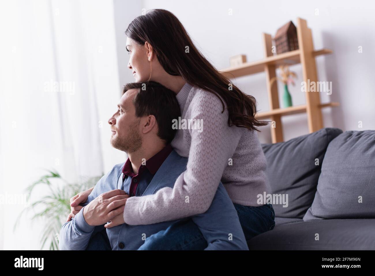 Woman embracing husband and looking away on couch Stock Photo - Alamy
