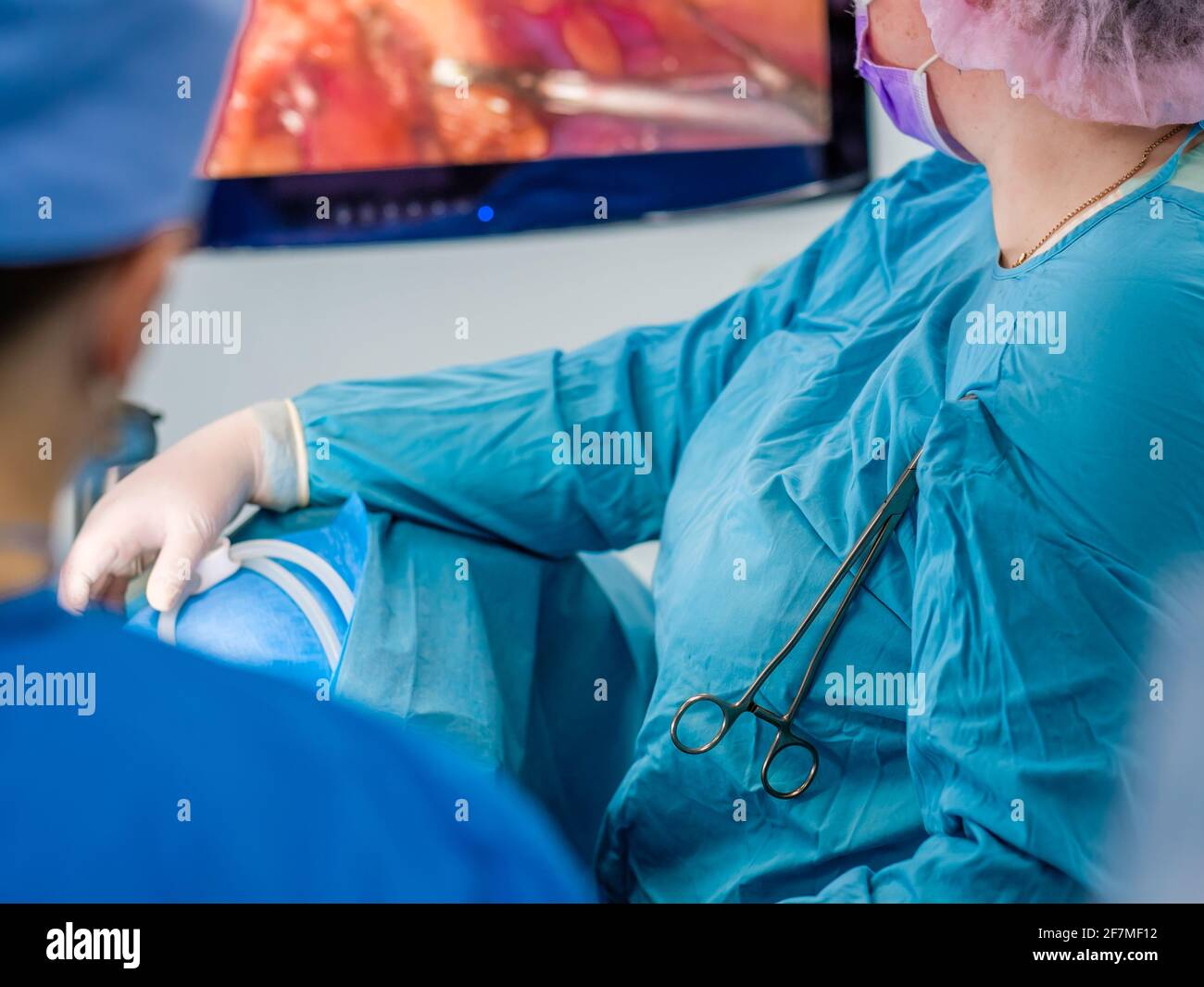 Selective focus on a surgical clamp on a blue gown of a doctor in a ...