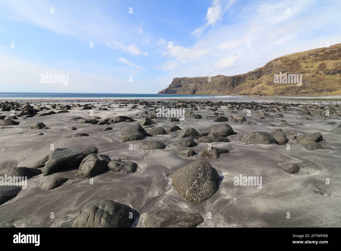 Large rocks on beach with cliff and rolling waves crashing on foreshore ...