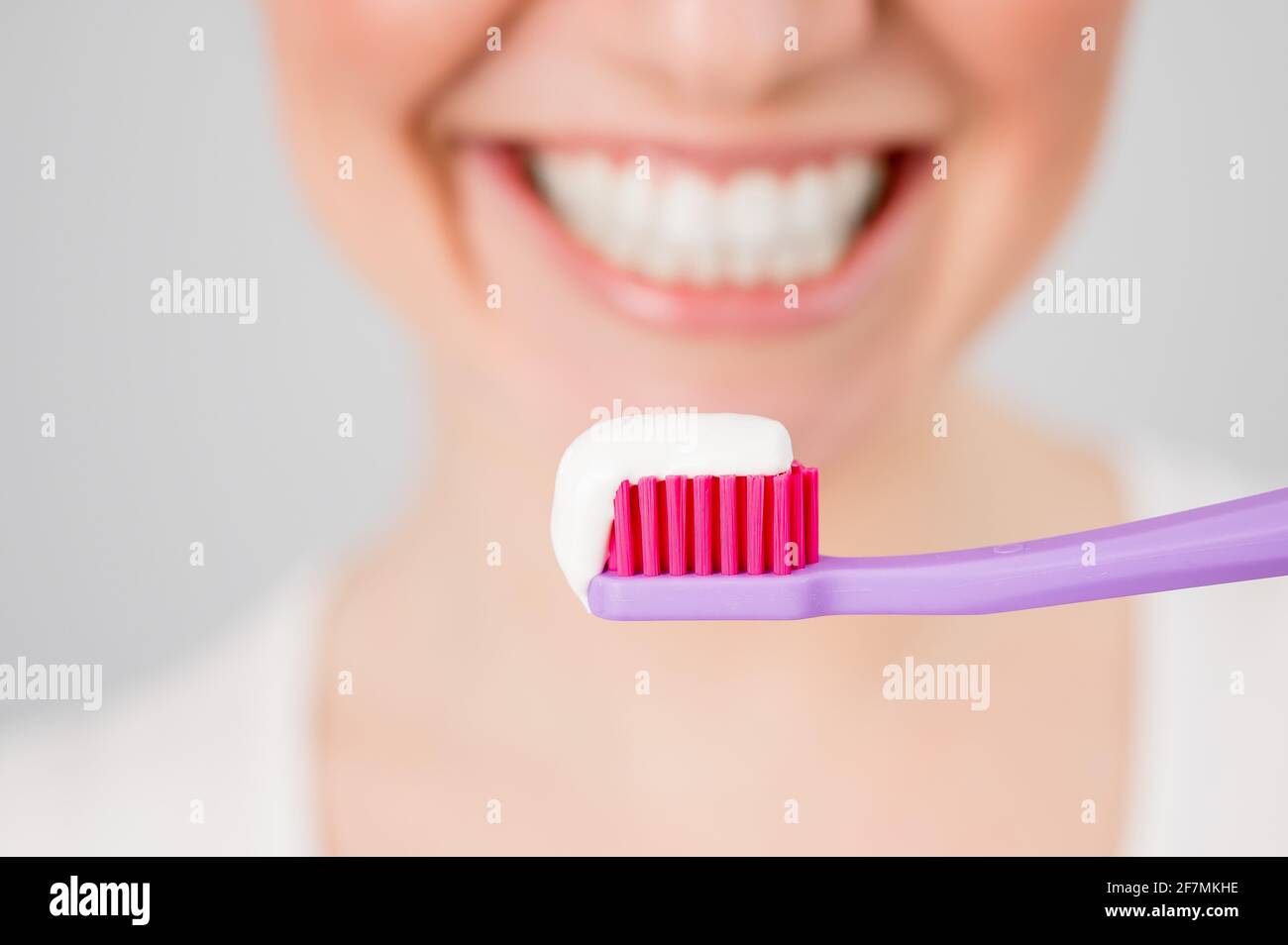 A woman with a snow-white smile holds a toothbrush with paste on a ...