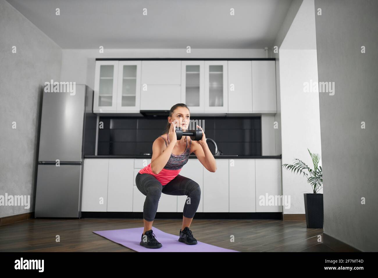 Side view of fit caucasian young woman squatting in kitchen. Strong ...