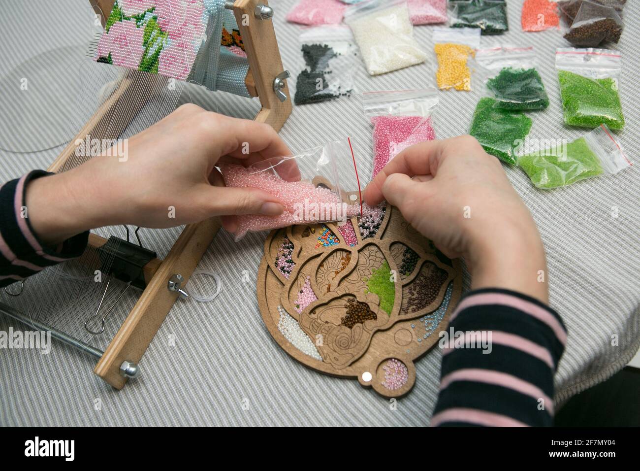 Weaving from beads. Close-up - a woman's hands are stringing beads on a ...
