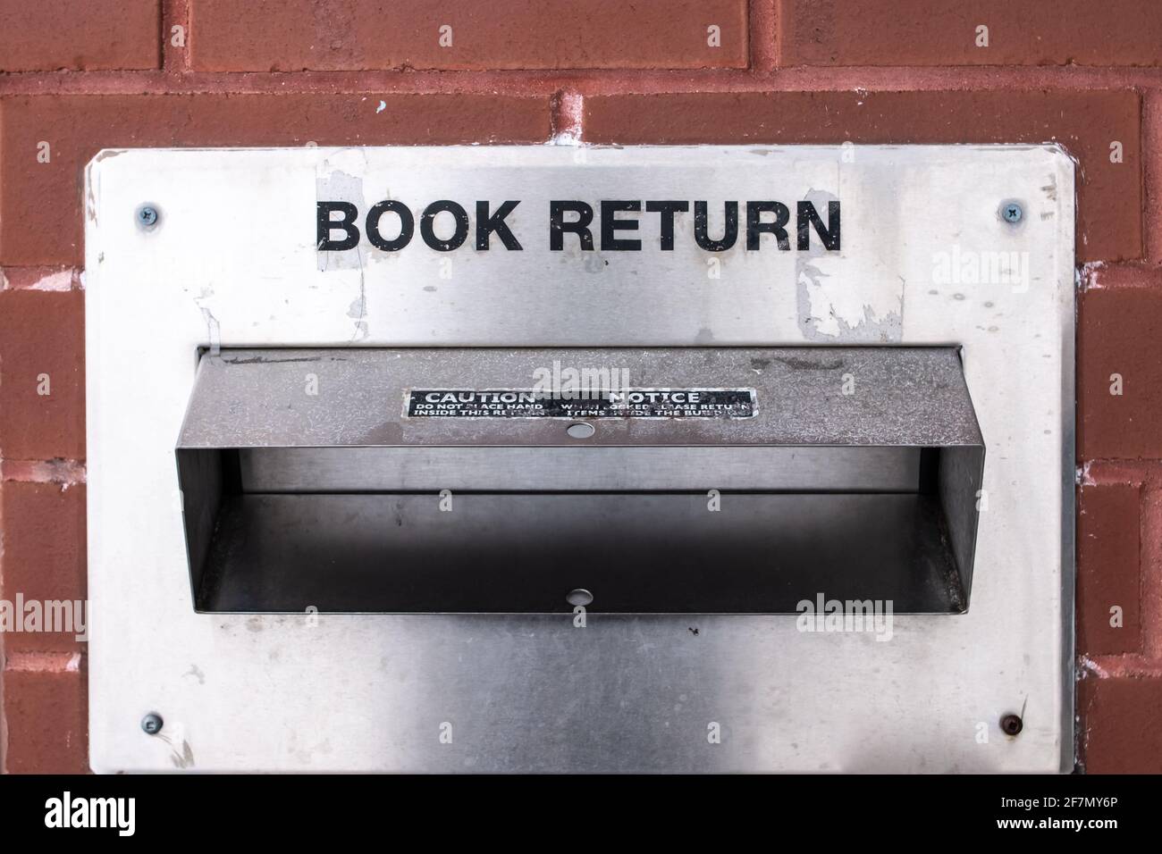 An old, weathered, aged metal book return container in a brick wall in ...