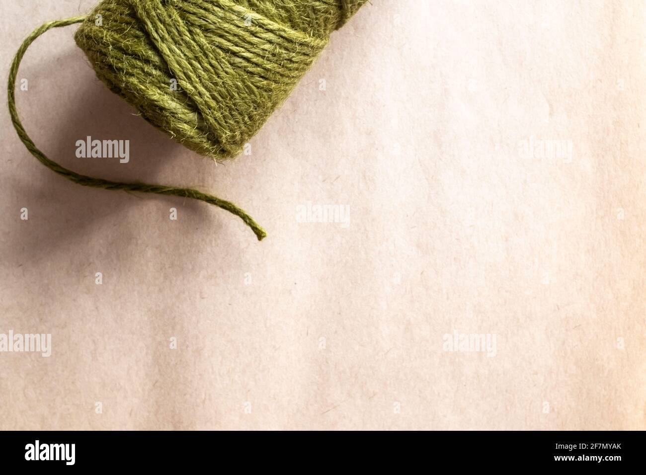 A cylinder of olive green yarn with a single strand hanging loose on a ...