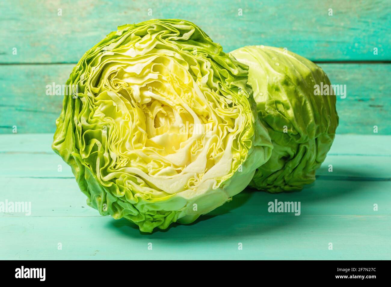 Fresh young cabbage, half and whole on bright green background. Modern ...